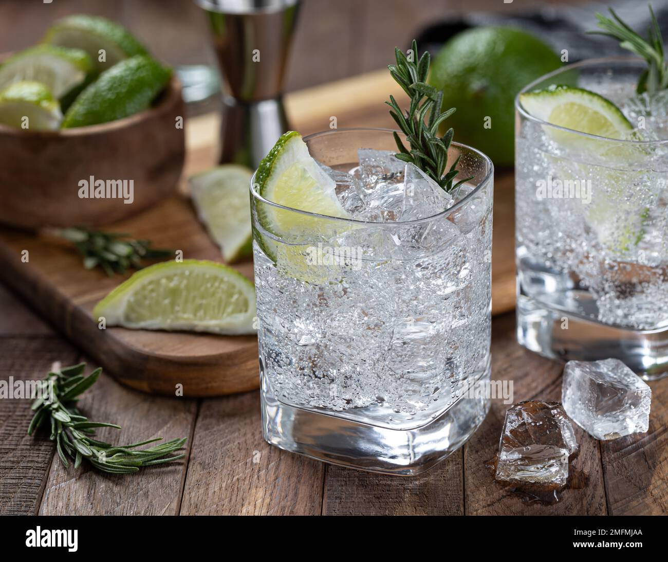 Gin and tonic cocktail with lime slices, rosemary and ice on a rustic ...