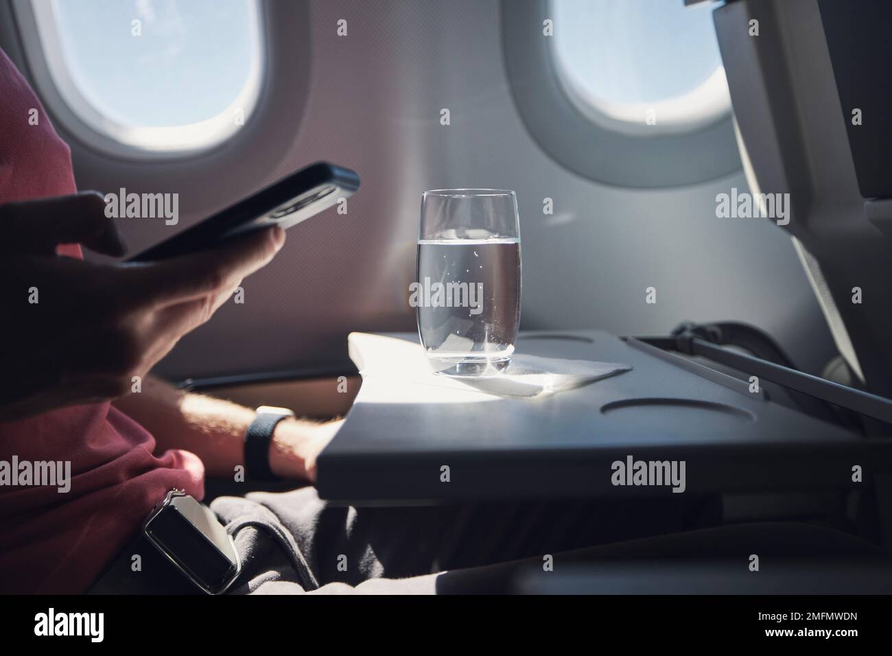 Glass of water on table of seat in airplane. Passenger is using phone ...