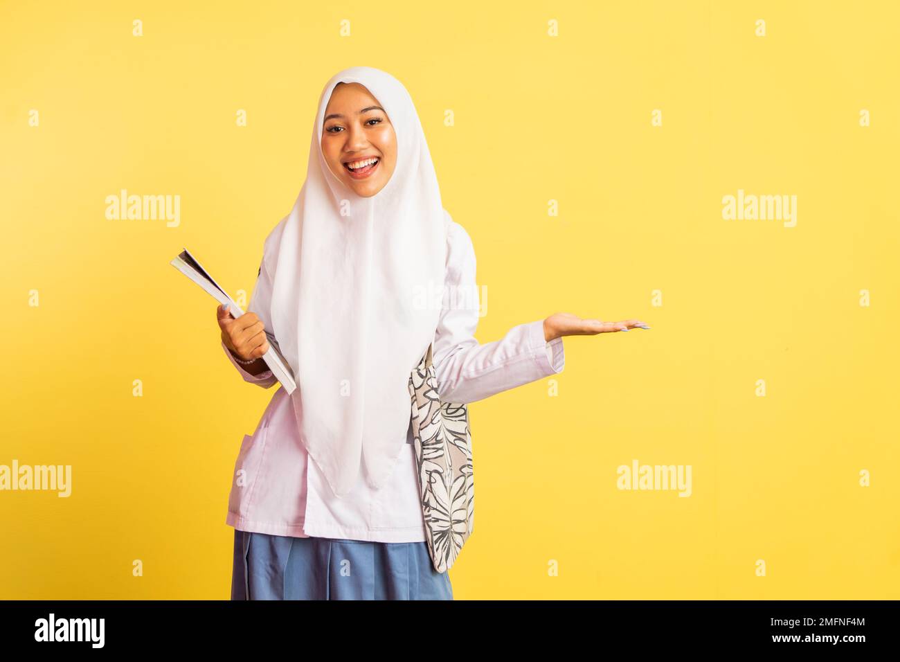 smiling student in hijab carrying book with gesture presenting ...