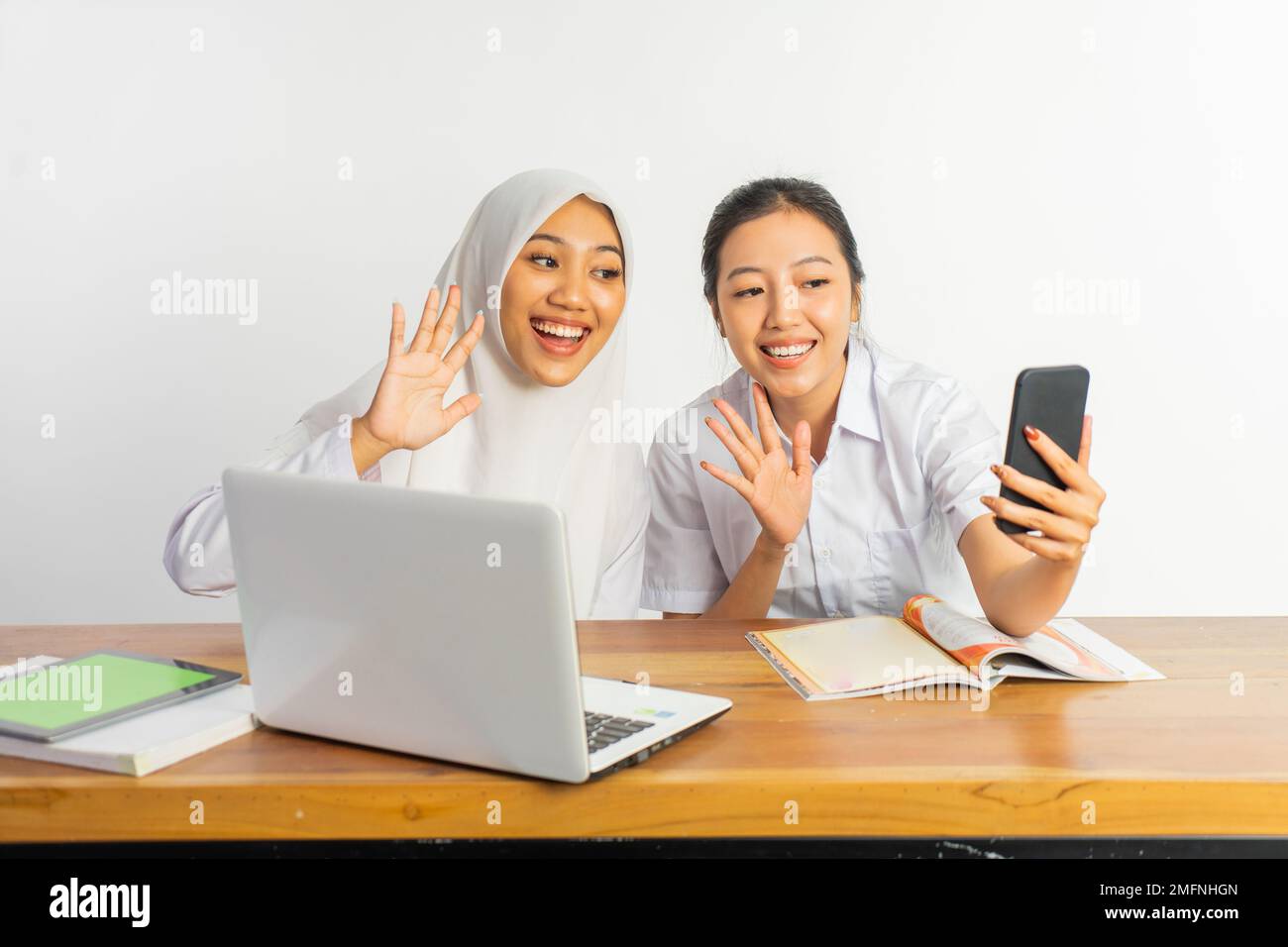 two waving high school girls at desk using mobile phones Stock Photo ...