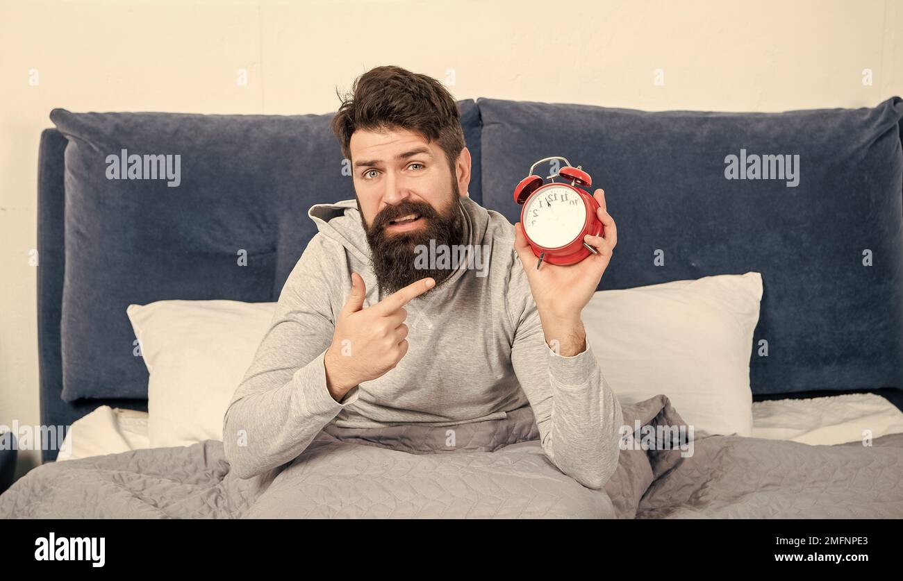 Sleepy man pointing finger at alarm clock being in bed awake, morning ...