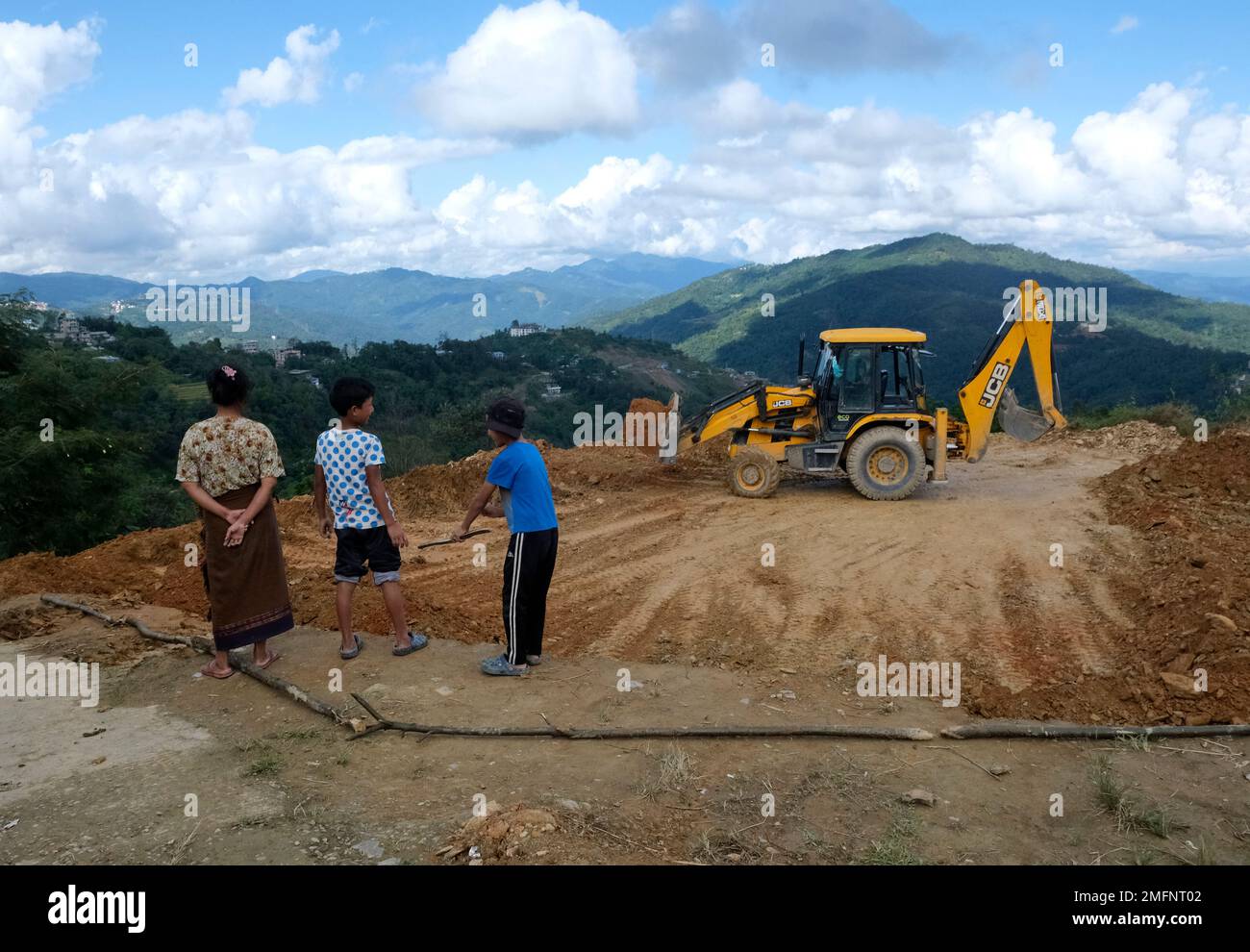 Naga children play while watching an earth mover level an area in ...