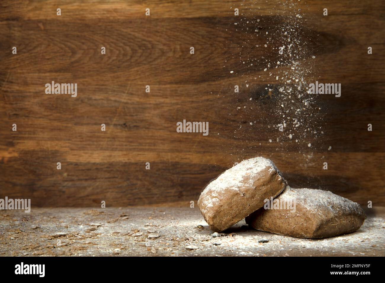 fresh baked whole grain bread on wooden background with falling flour ...