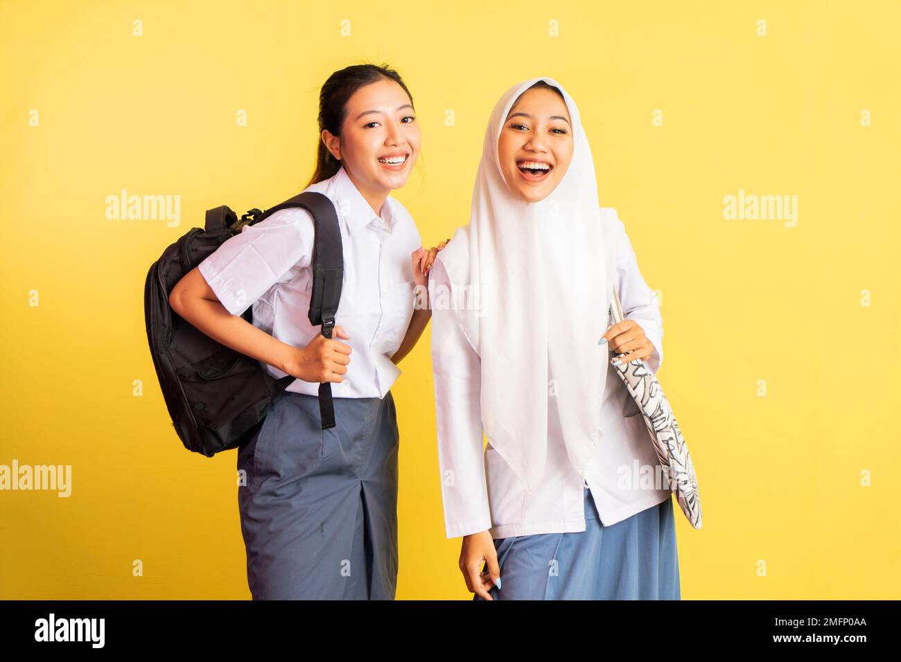 two high school girls laughing at camera while carrying bags Stock ...