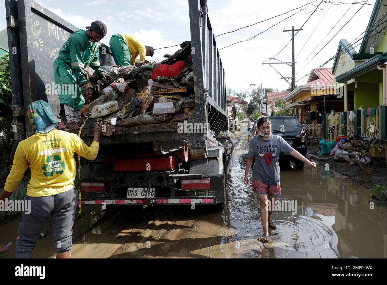 Workers collect garbage along a mud-covered road after floodwaters ...