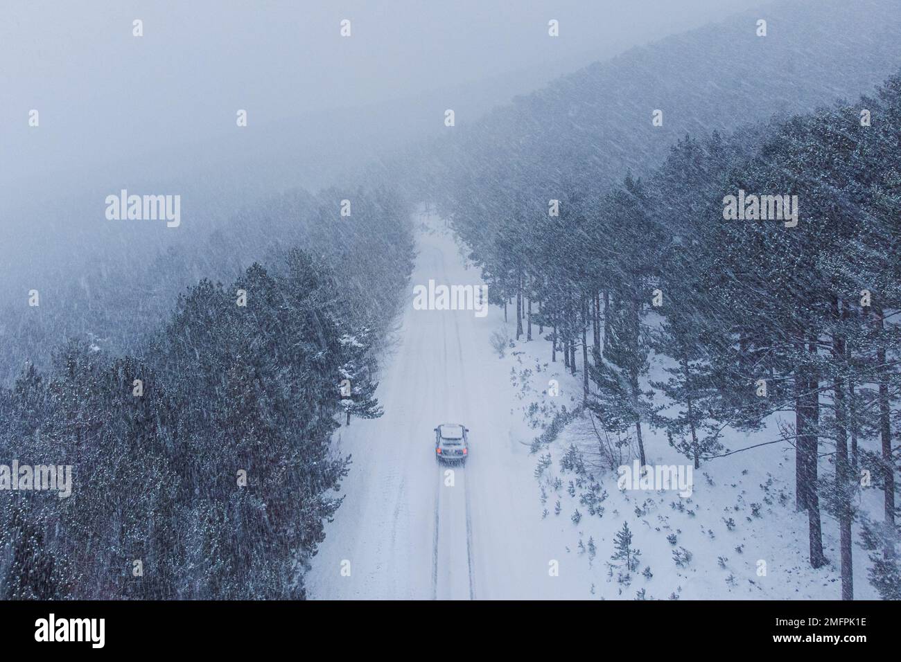An aerial view of a car driving on a road cover in snow during a ...