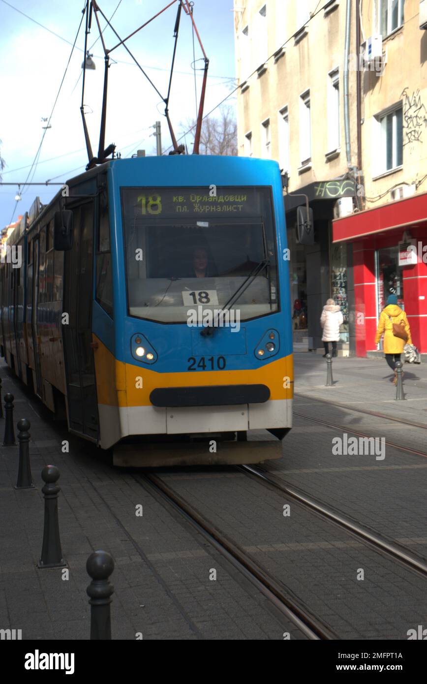 A vertical shot of a tram passing through narrow street with buildings ...