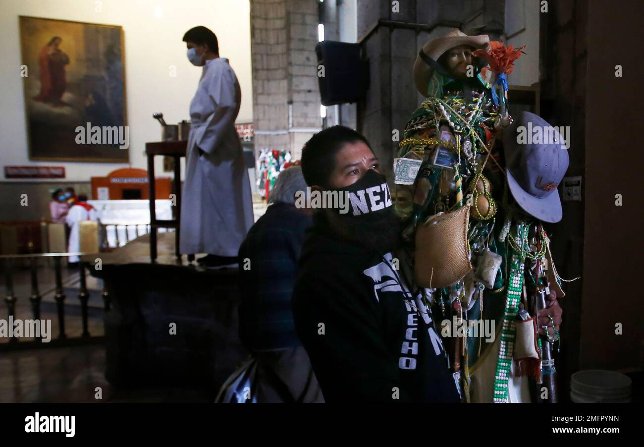 A devotee carrying a Saint Jude statue and wearing protective face ...