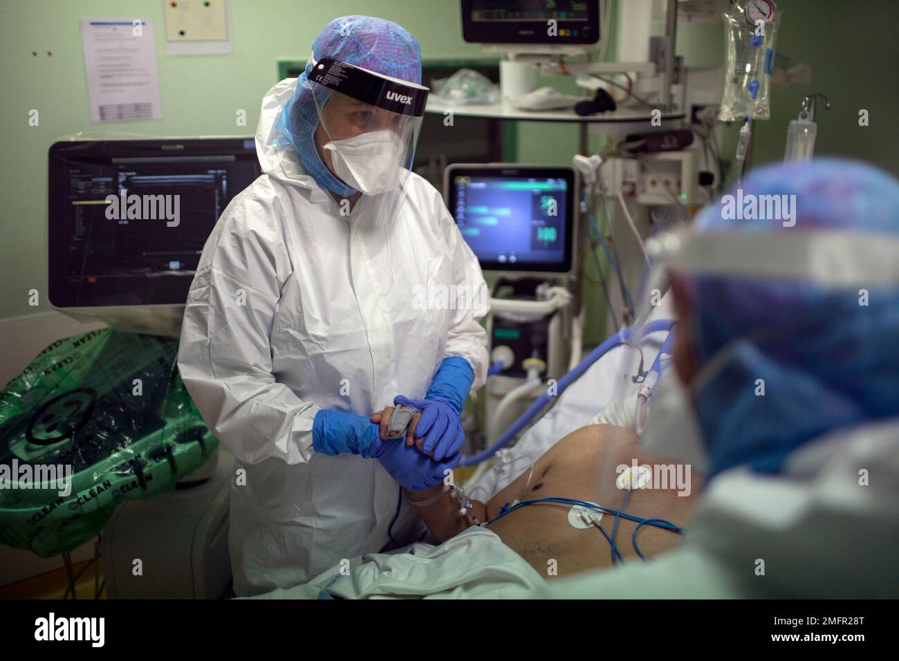 A nurse holds the hand of a COVID-19 patient in the intensive care unit ...