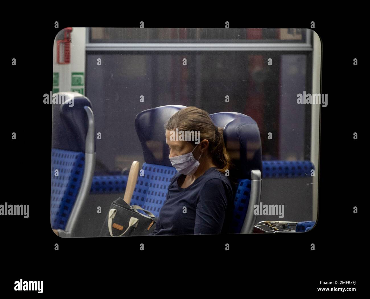 A woman wearing a face mask sits in a train in the main station in ...