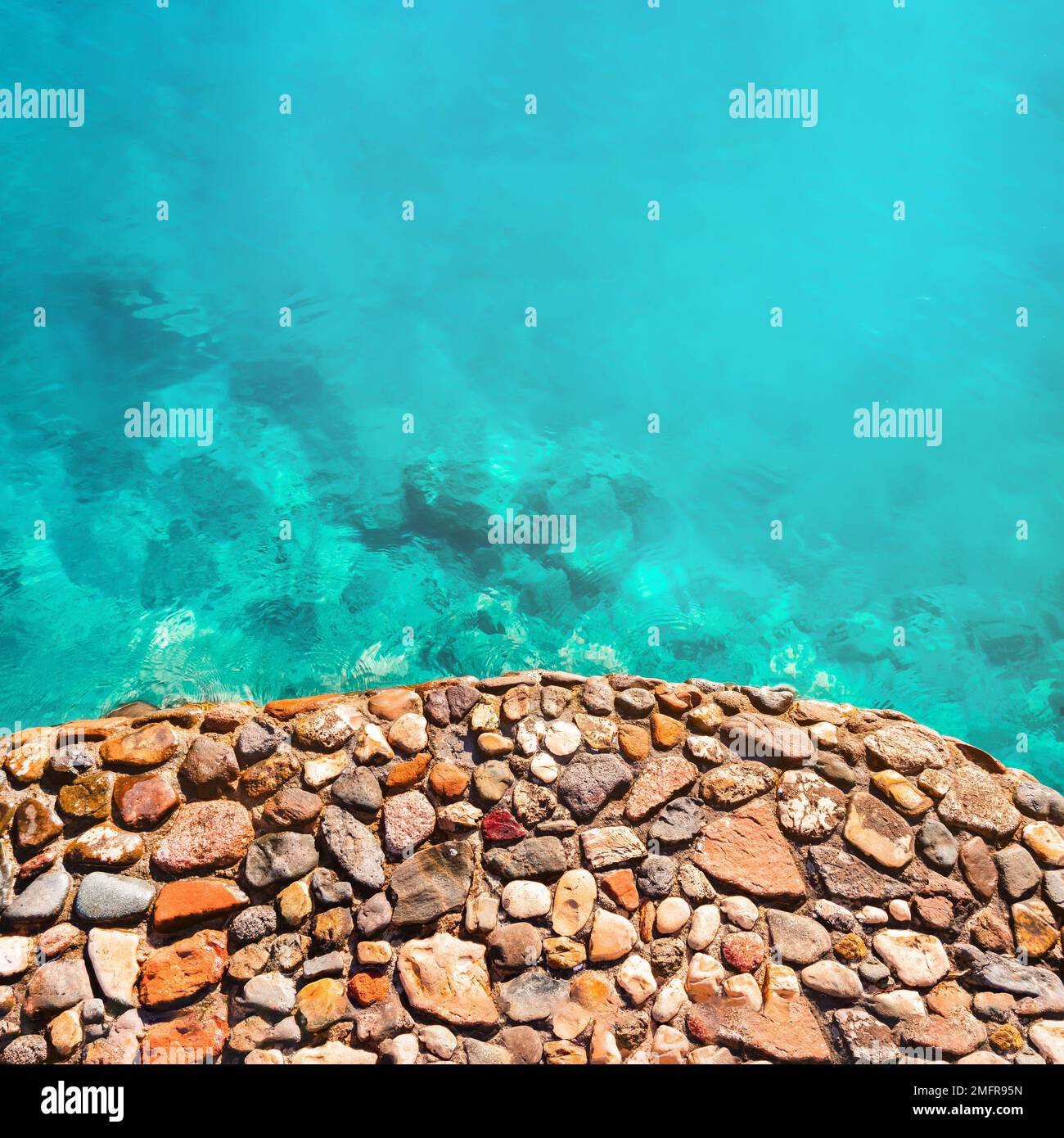 The transparent blue sea approaches the multi colored stone shore. The ...