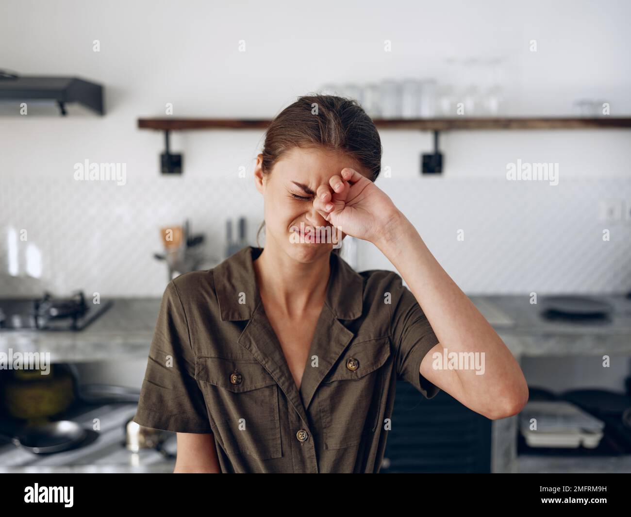 Portrait of a sad tired woman with a sore head in the kitchen, domestic ...