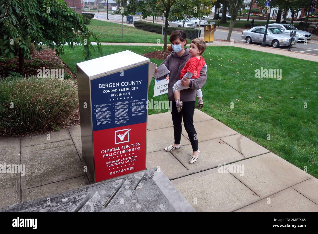 A woman in a face mask carrying a child drops a ballot in a drop box in ...