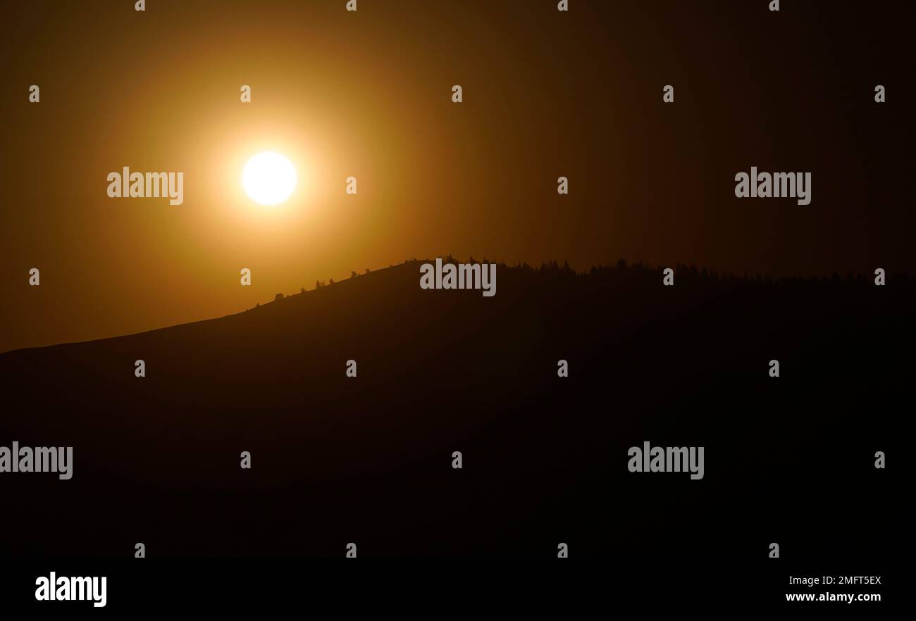 Smoke obscures the sun as it sets behind a mountain ridge as a wildfire ...