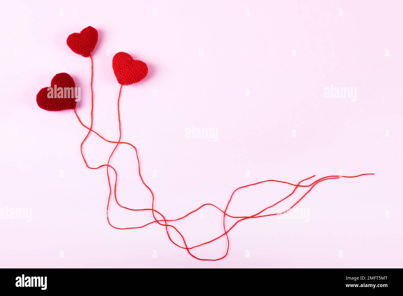 Red crocheted hearts are laid out in the shape of a balloons on a pink ...