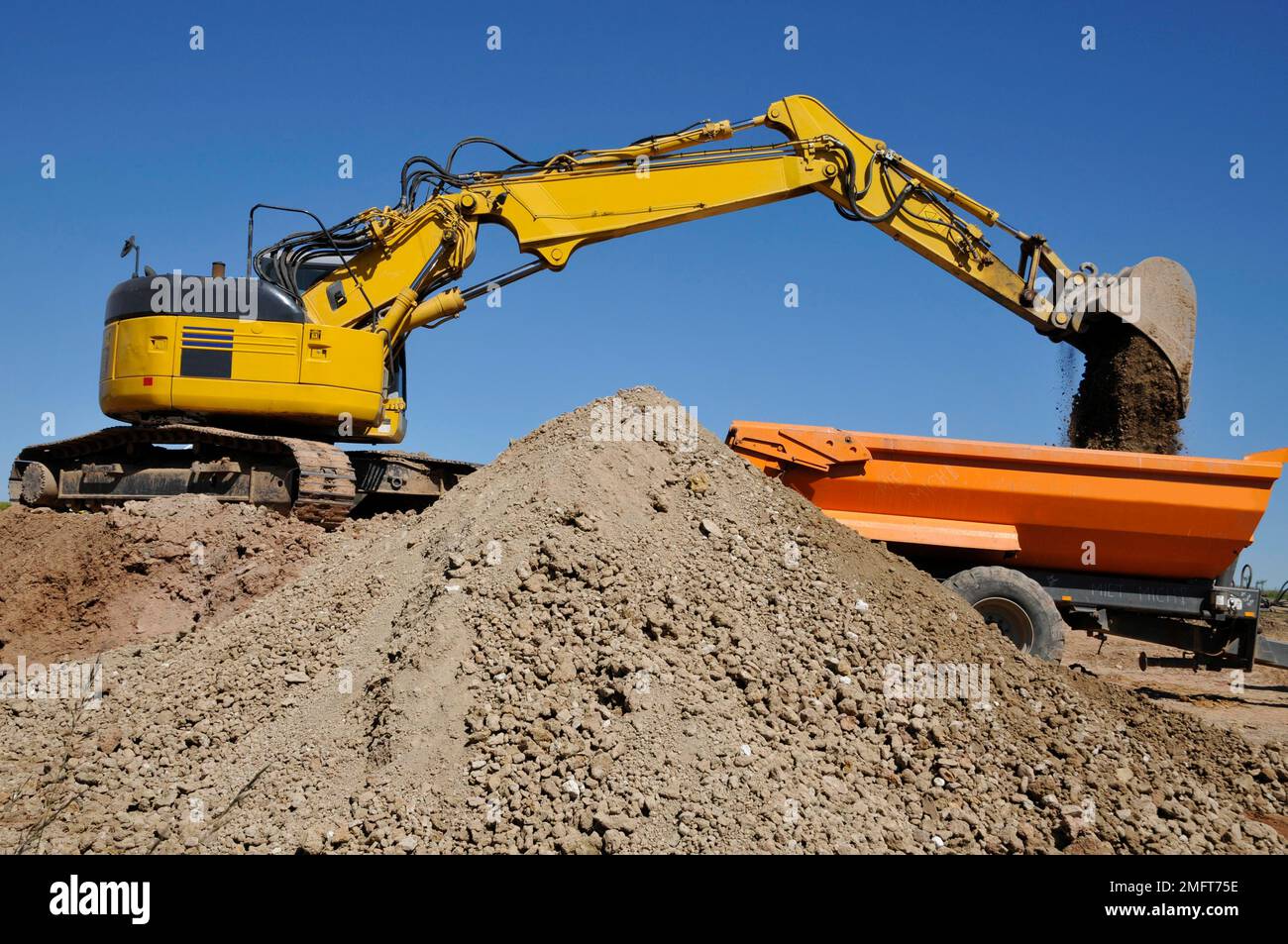 Excavator loading trailers with earth and gravel at a construction site ...