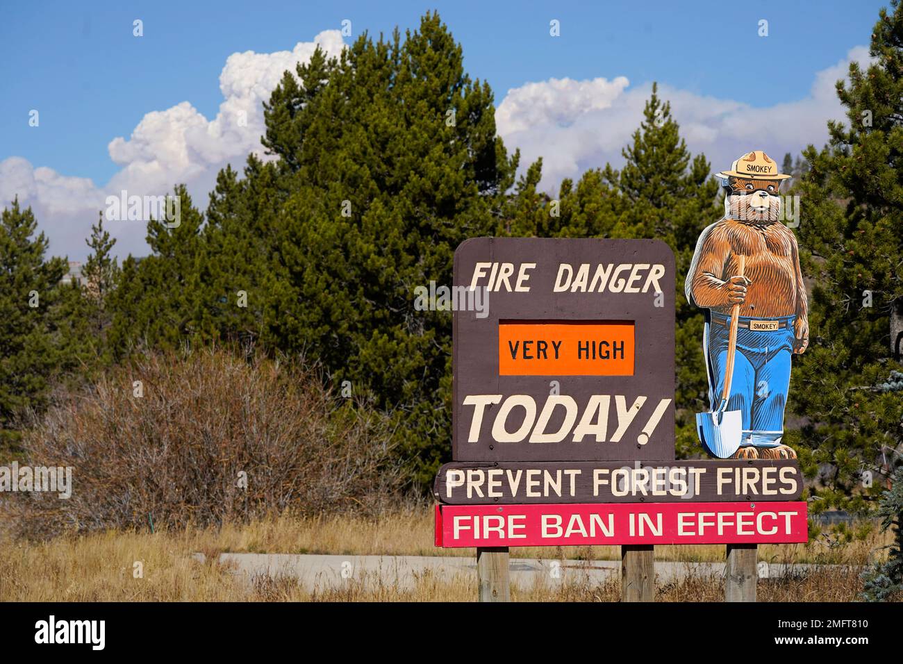 Smoke rises from mountain ridges while a sign warns of fire danger as a ...