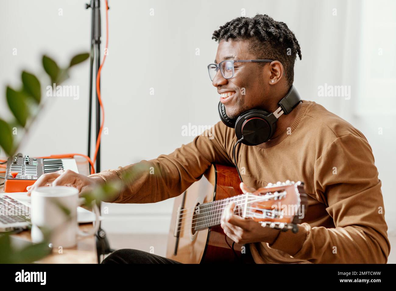 side view smiley male musician home playing guitar mixing with laptop ...