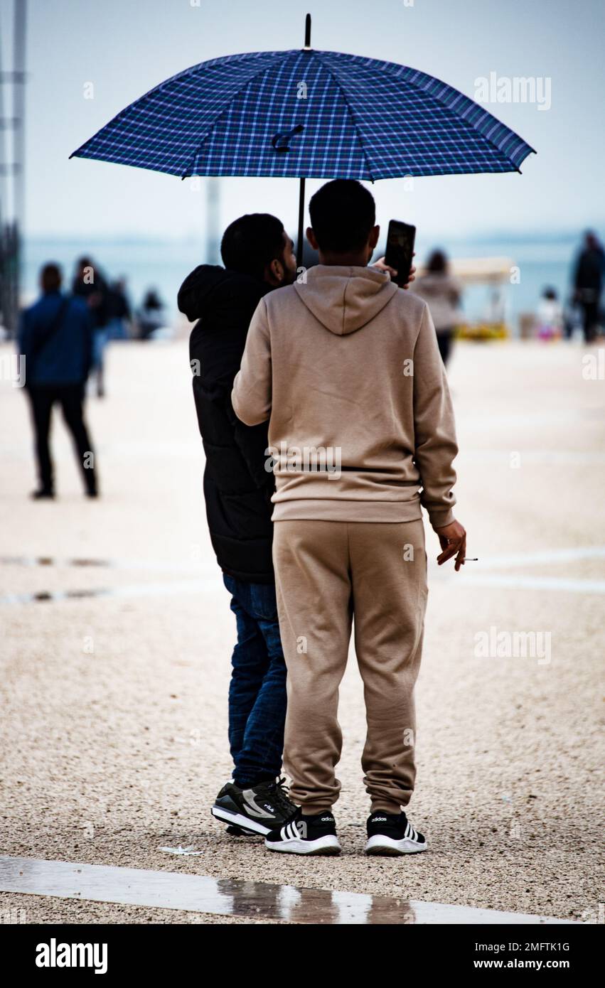 Two men take shelter from the rain with an umbrella Stock Photo - Alamy