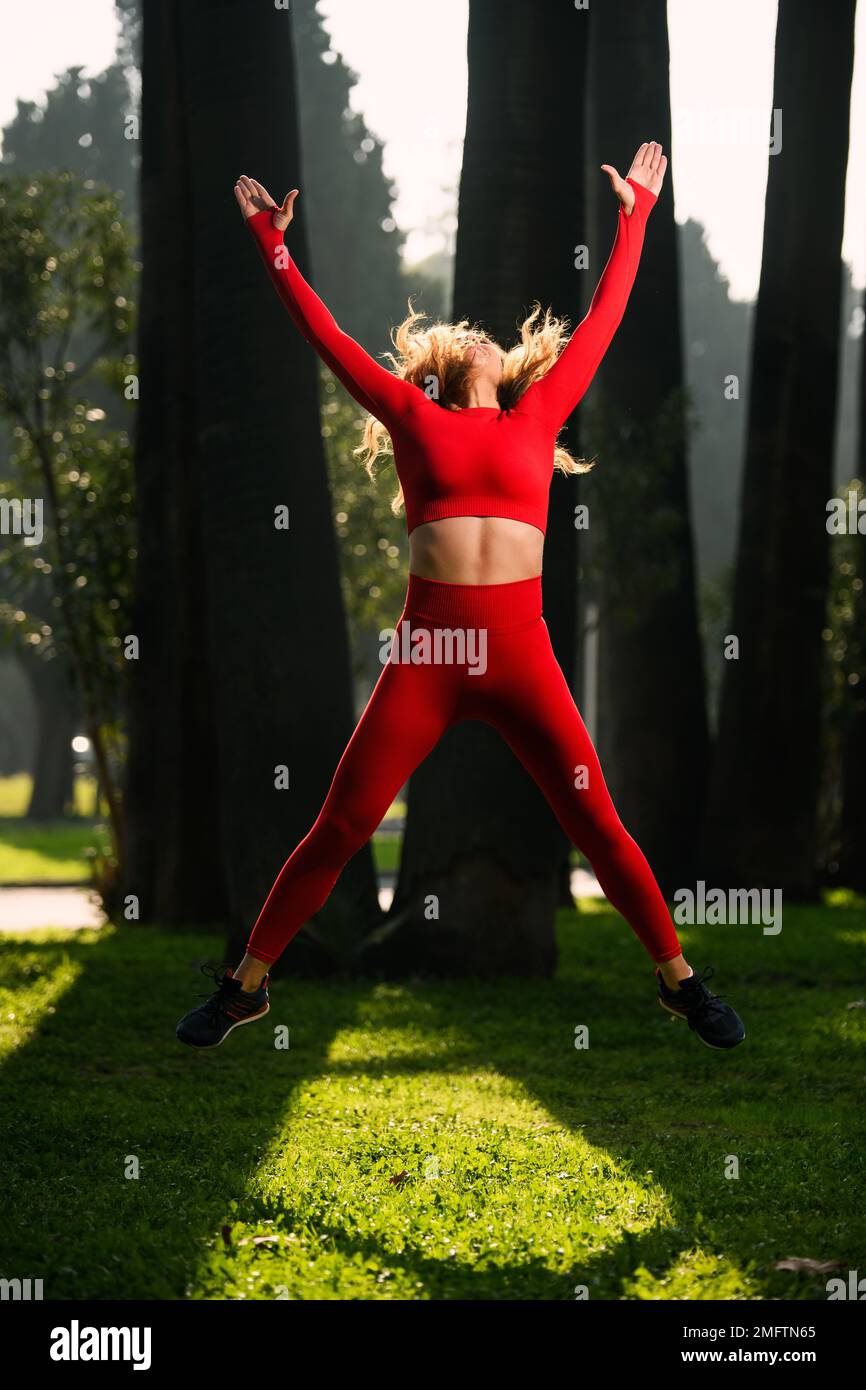 Jumping woman with an x form with yoga tights and tops in a public park ...