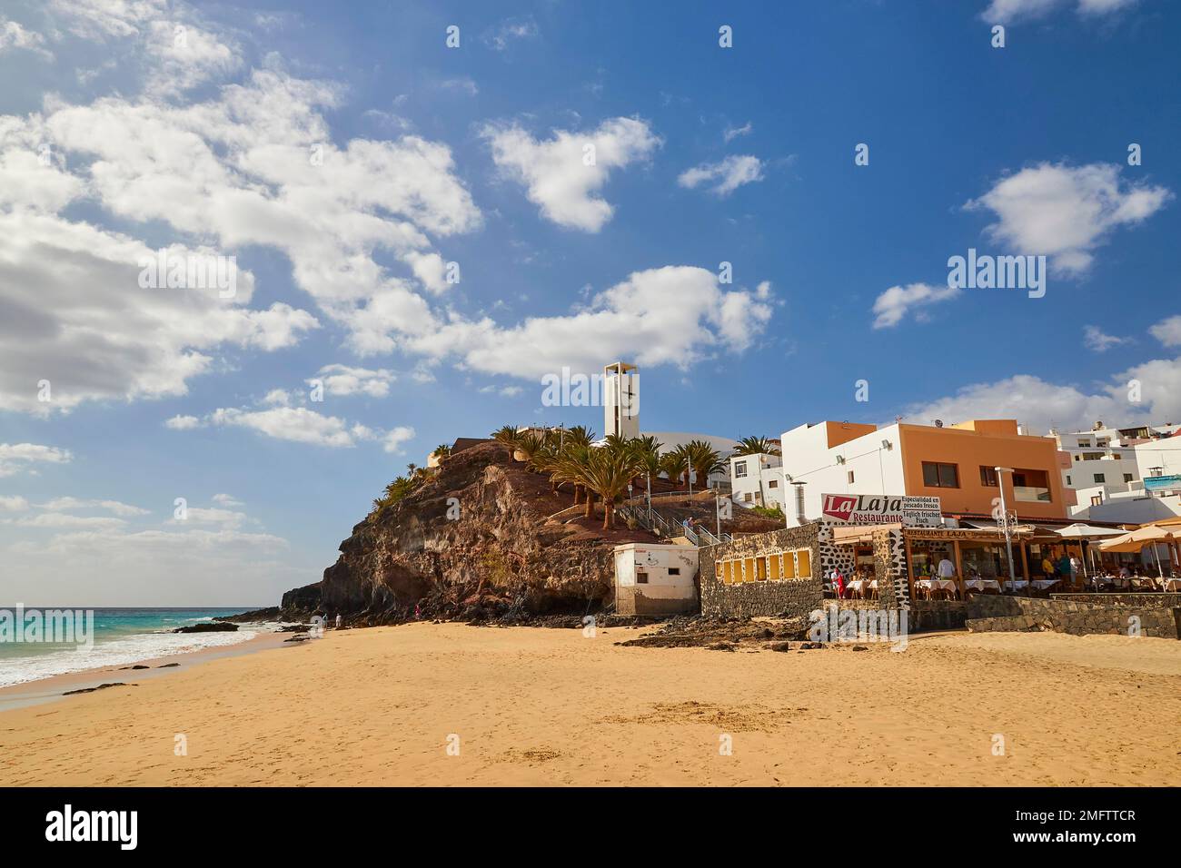 Sandy beach beach, church tower, restaurant, houses, palm trees, hills ...