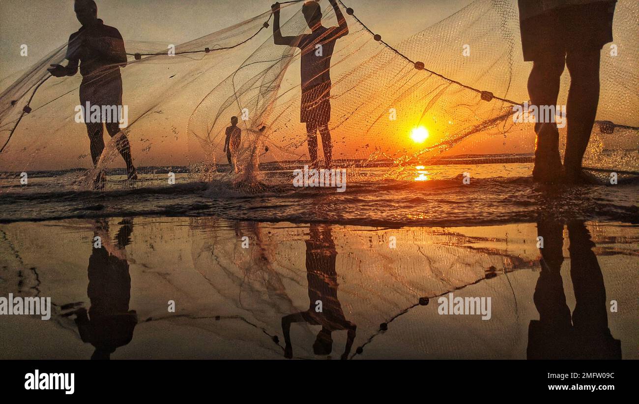 Silhouetted fishermen and their net on a beach at dusk Stock Photo - Alamy