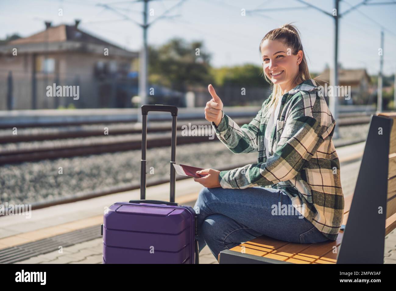 Happy woman showing thumb up and holding ticket while sitting on bench ...