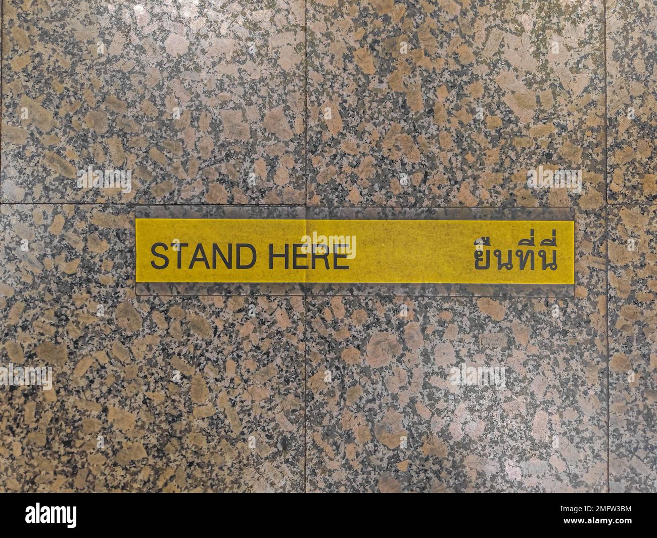 Stand here sign on the floor showing where to stand in English and Thai ...
