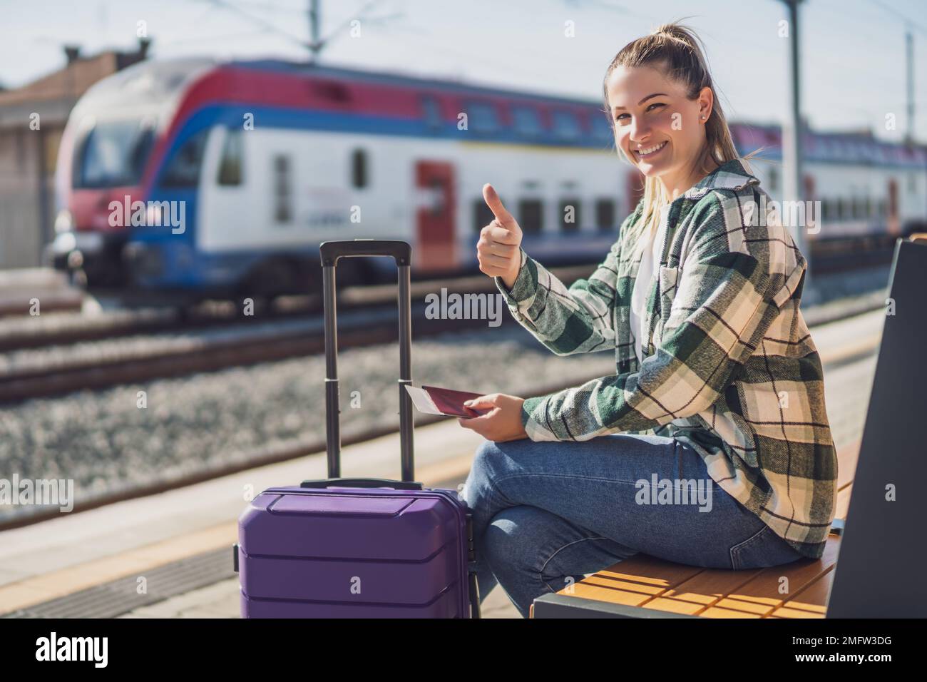 Happy woman showing thumb up and holding ticket while sitting on bench ...
