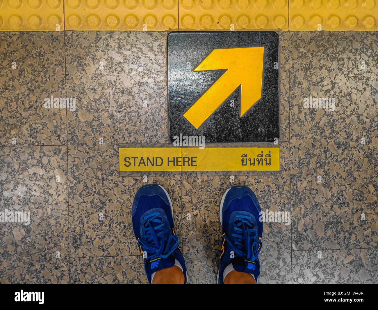 Man standing in front of Stand here sign on the floor showing where to ...