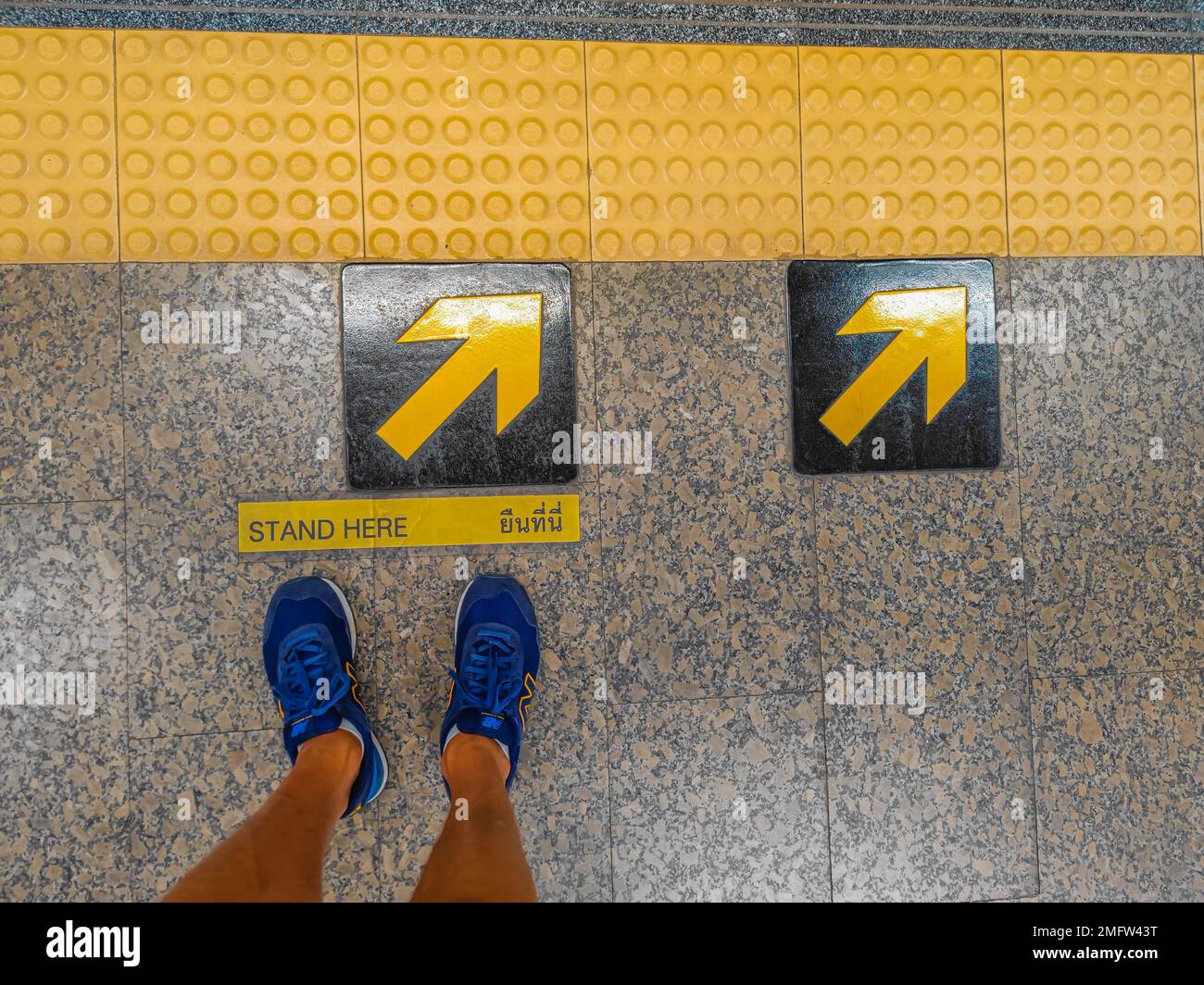 Man standing in front of Stand here sign on the floor showing where to ...