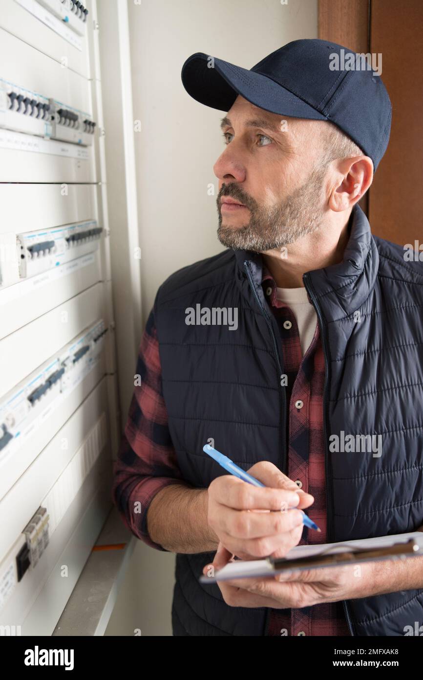 male technician writing on clipboard in front of fuse box Stock Photo ...
