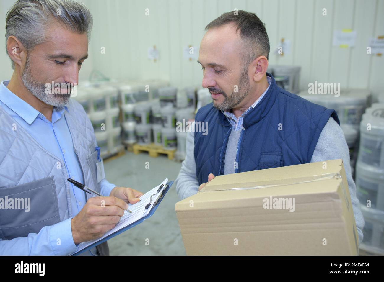 two couriers with a parcel signing a delivery form Stock Photo - Alamy