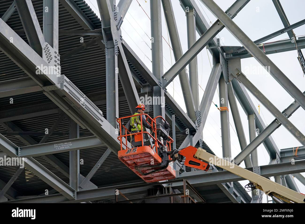 A worker uses a lift to elevate himself to the upper beams as ...