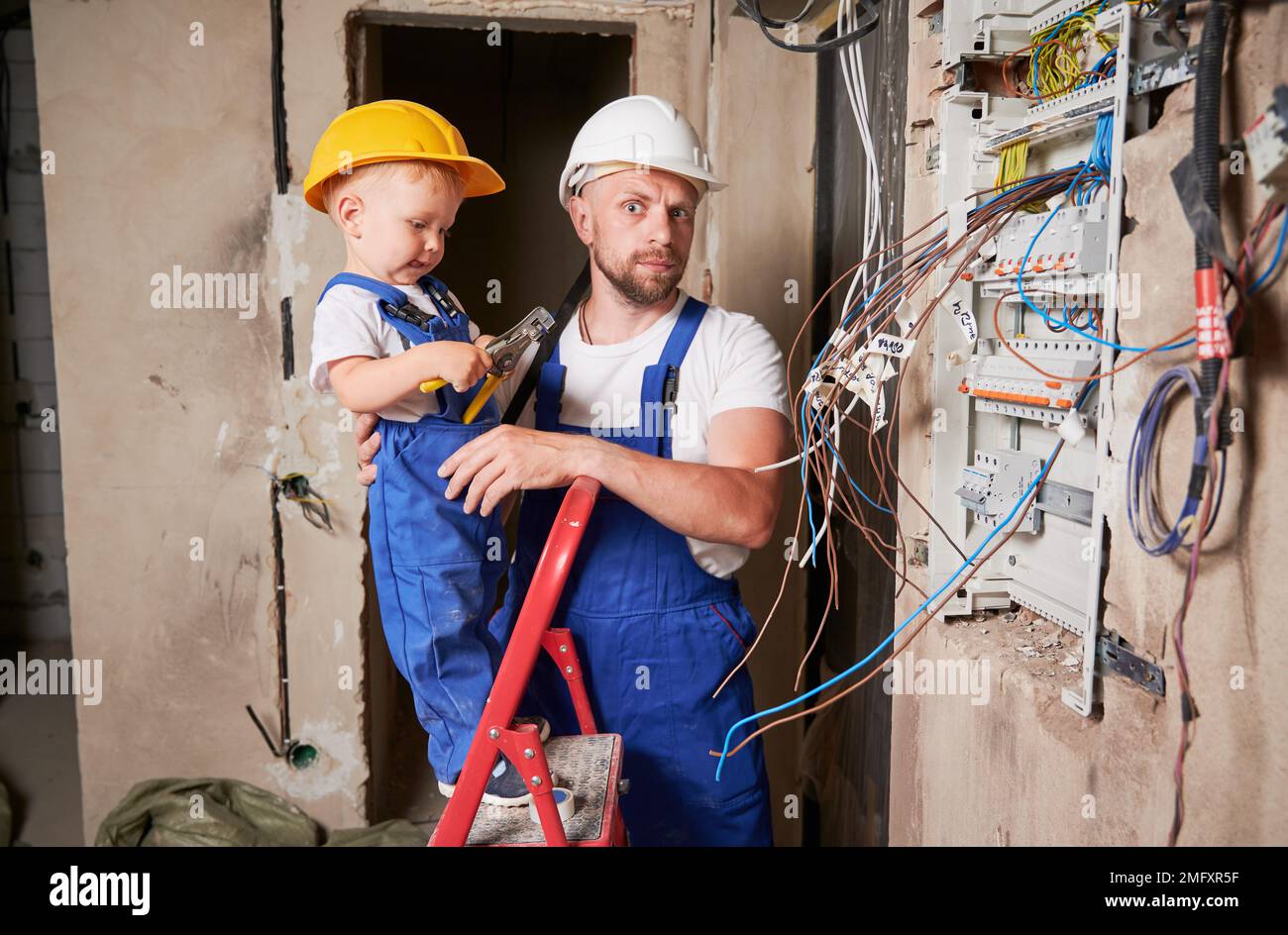 Child electrician standing in ladder and holding pliers tool while ...