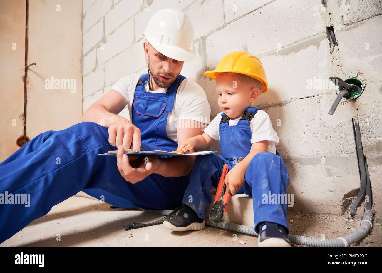Male worker sitting by brick wall and pointing at clipboard while ...