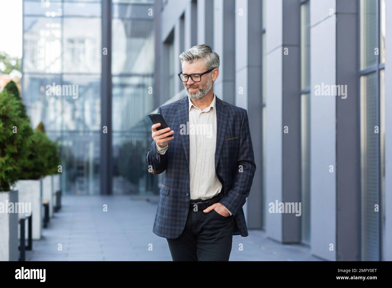 Successful gray-haired businessman walks outside office building ...