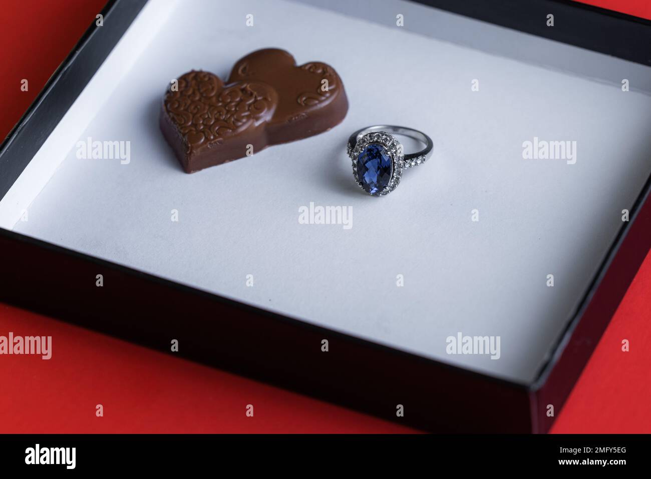 Blue sapphire ring with chocolates inside a white box on a red ...