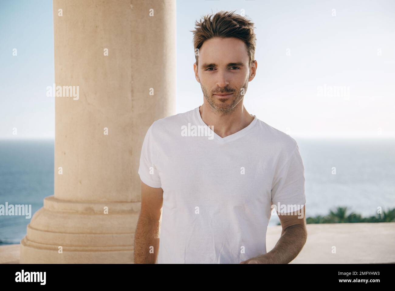 Young handsome guy standing on a open balcony. Man is wearing white ...