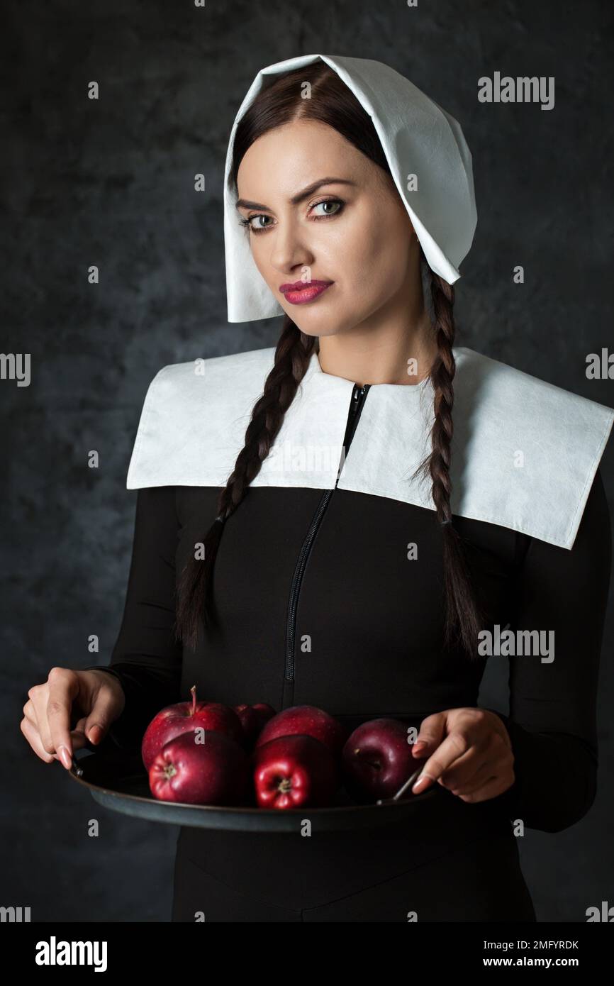 Gothic woman with pigtails holds a tray with red apples on a dark ...