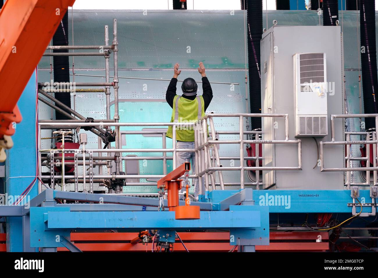 A worker motions as he stands on a platform next to a Boeing 787 ...