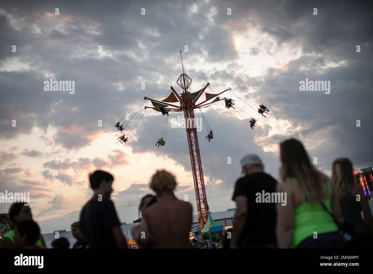 Visitors are silhouetted against an amusement ride at the Perry State ...