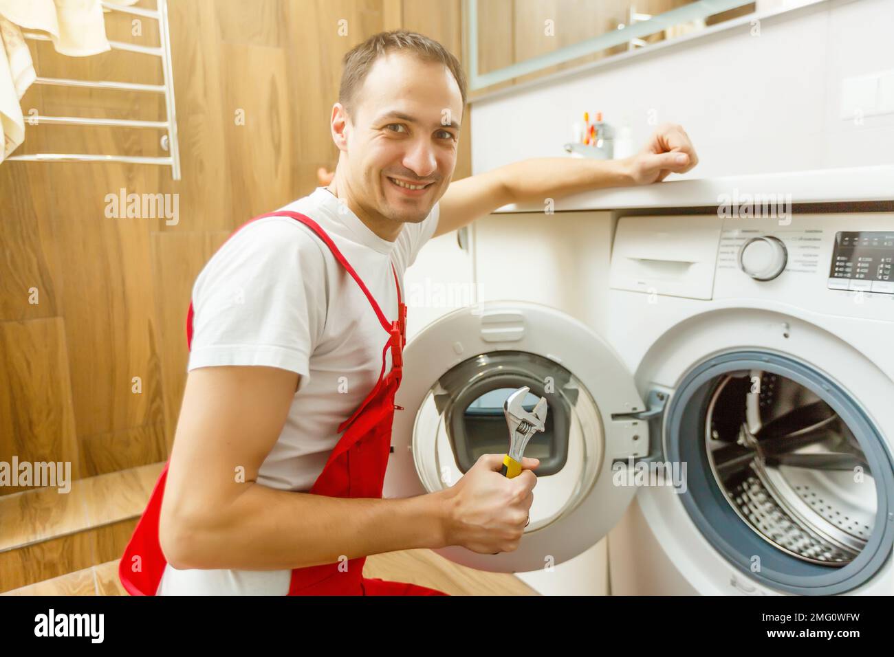 Young attractive smiling worker in uniform fixing washing machine ...