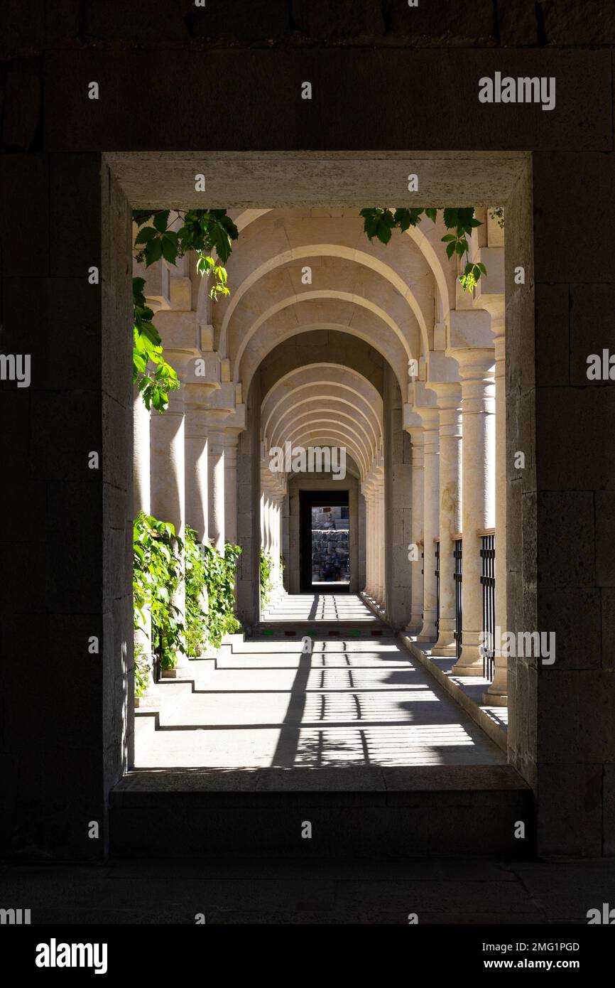 Symmetrical stone passageway with repeating arches, white columns and ...