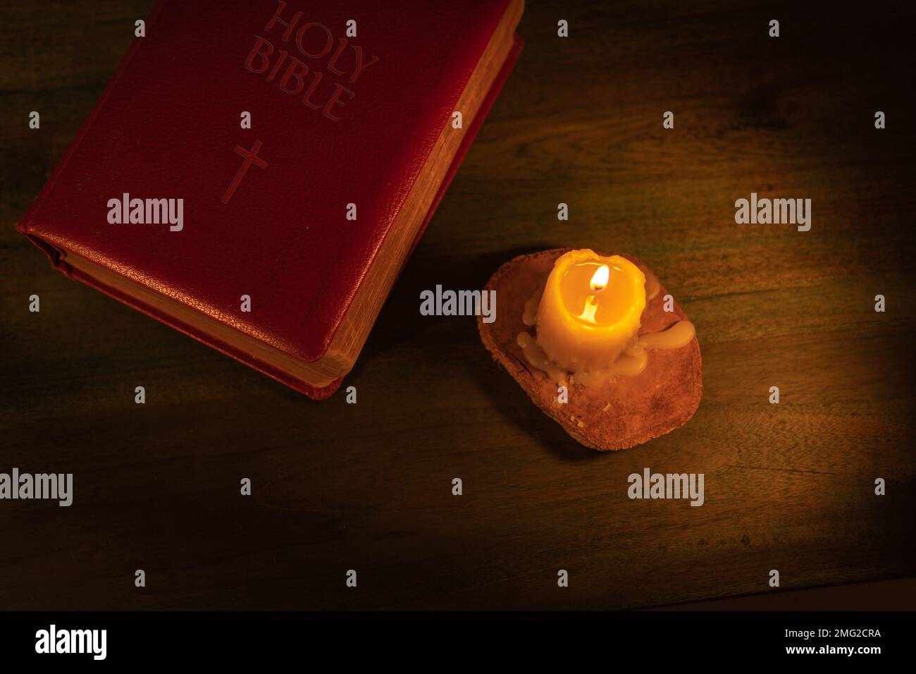 Top view of a closed bible illuminated with a lit candle on a wooden ...