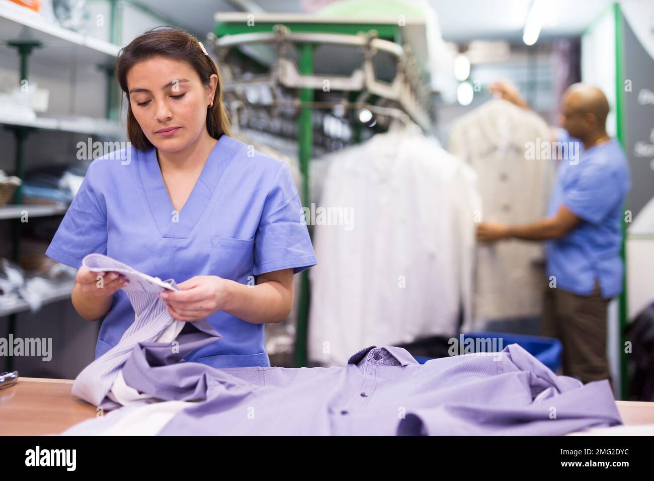 Focused woman dry-cleaning worker checking clean clothes Stock Photo ...