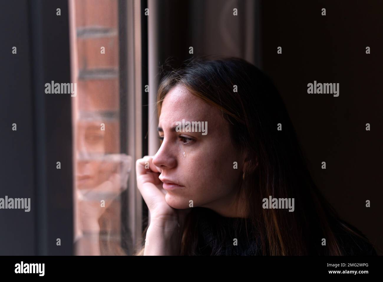 Side view of lonely lady with dark hair looking out of window and ...