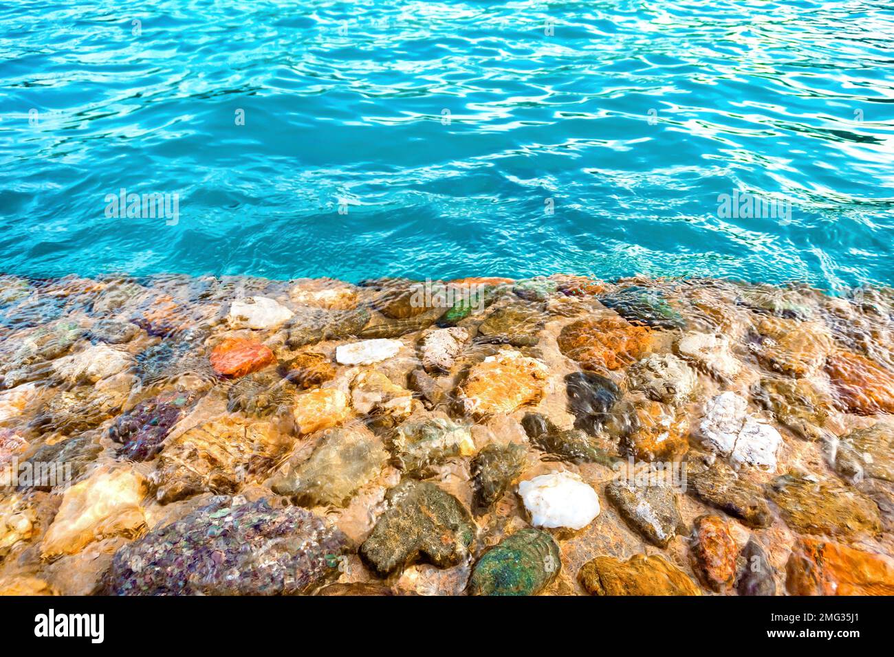 The shore of beautiful multicolored stones washed by clear blue water ...