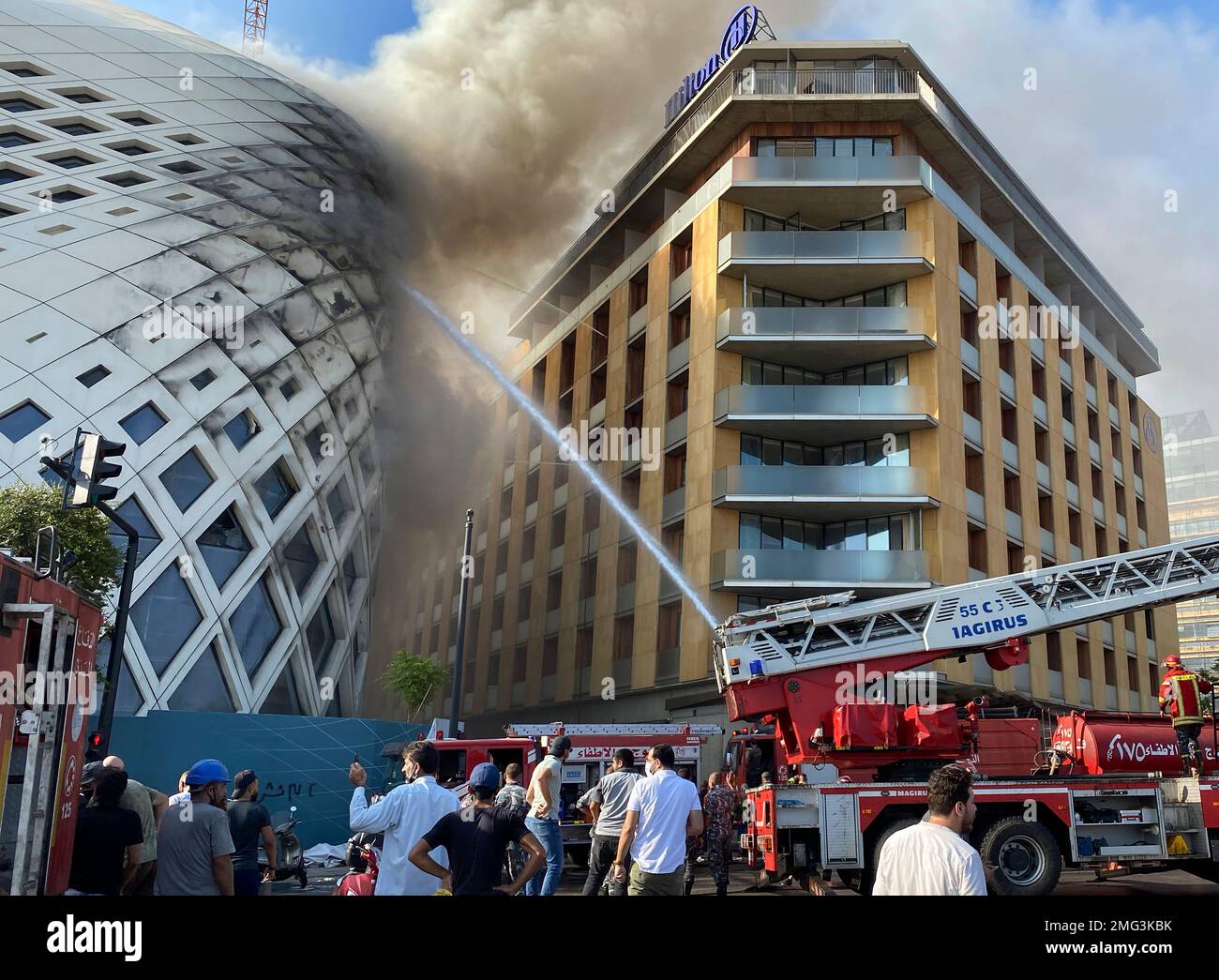 People gather next of firefighters who are extinguish a building under ...