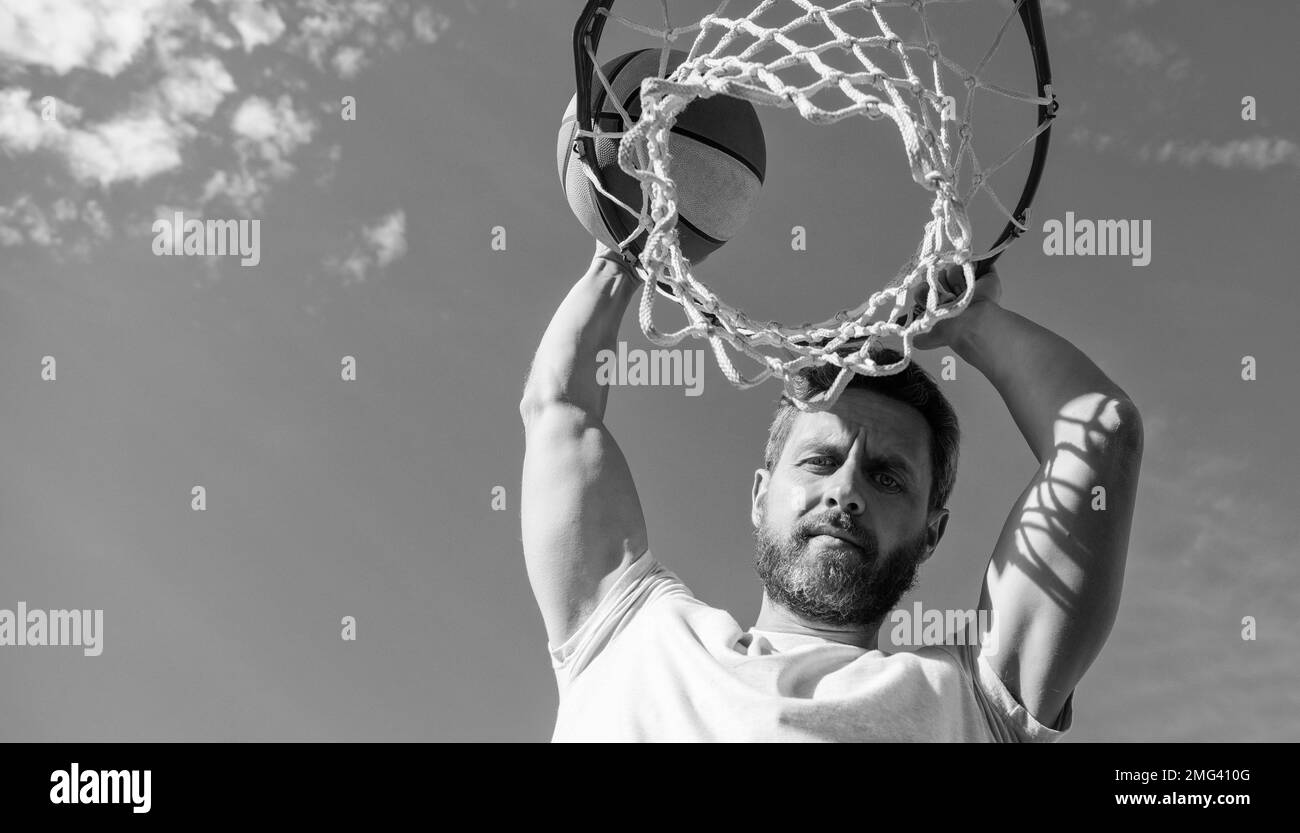 man dunking basketball ball through net ring with hands, copy space ...